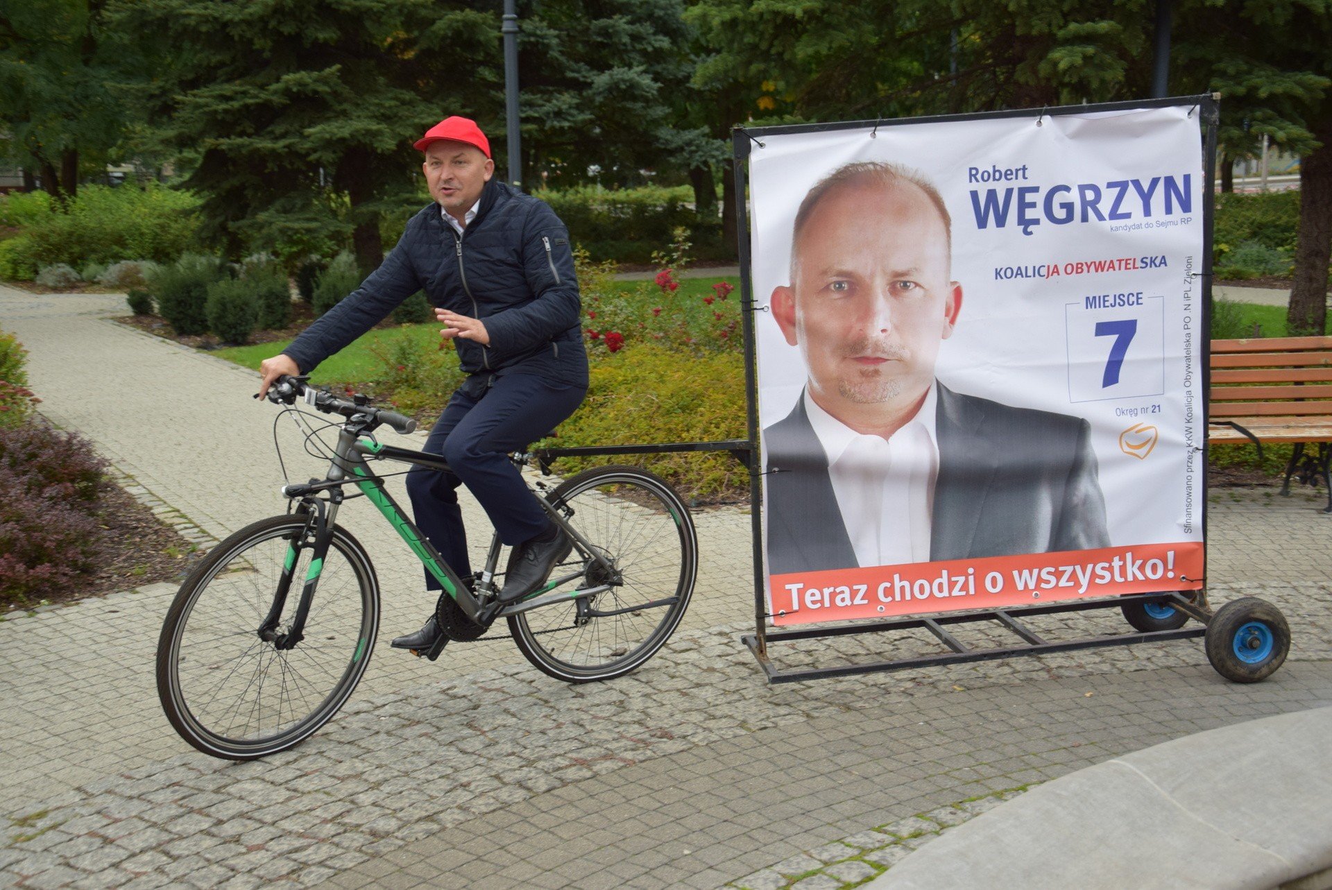 Robert Węgrzyn ciągnie na rowerze przyczepkę ze swoim banerem wyborczym ...